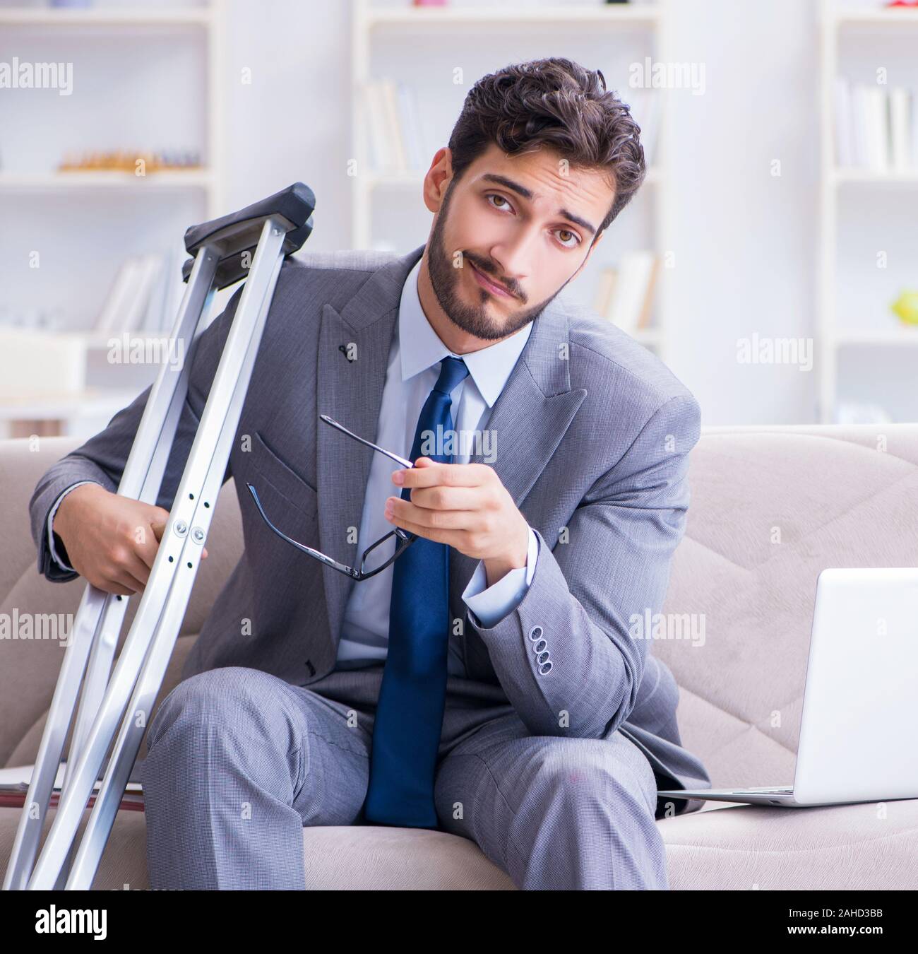 The businessman with crutches and broken leg at home working Stock ...