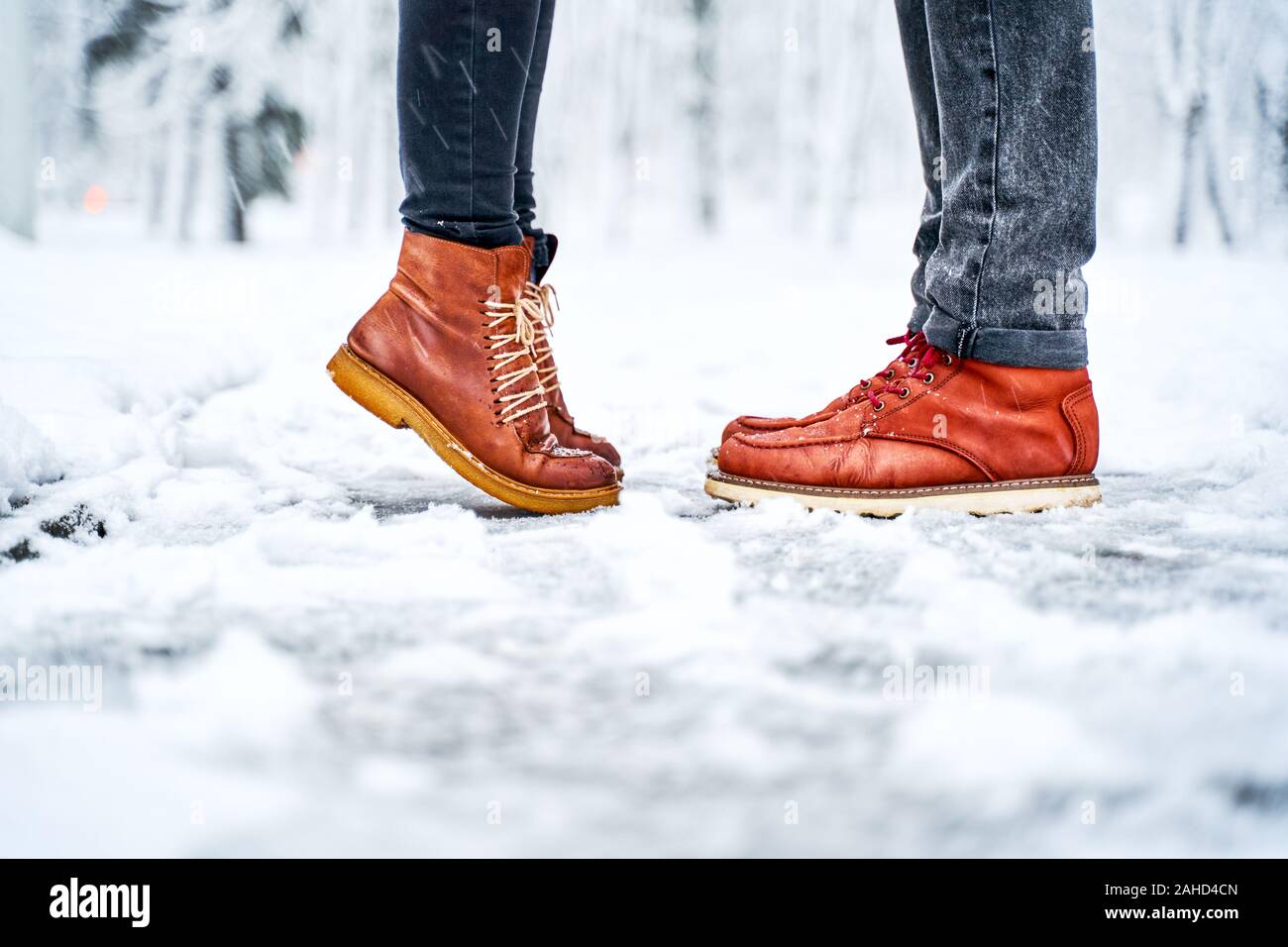Feet of a couple on a snowy sidewalk in brown boots. Girl stands on ...