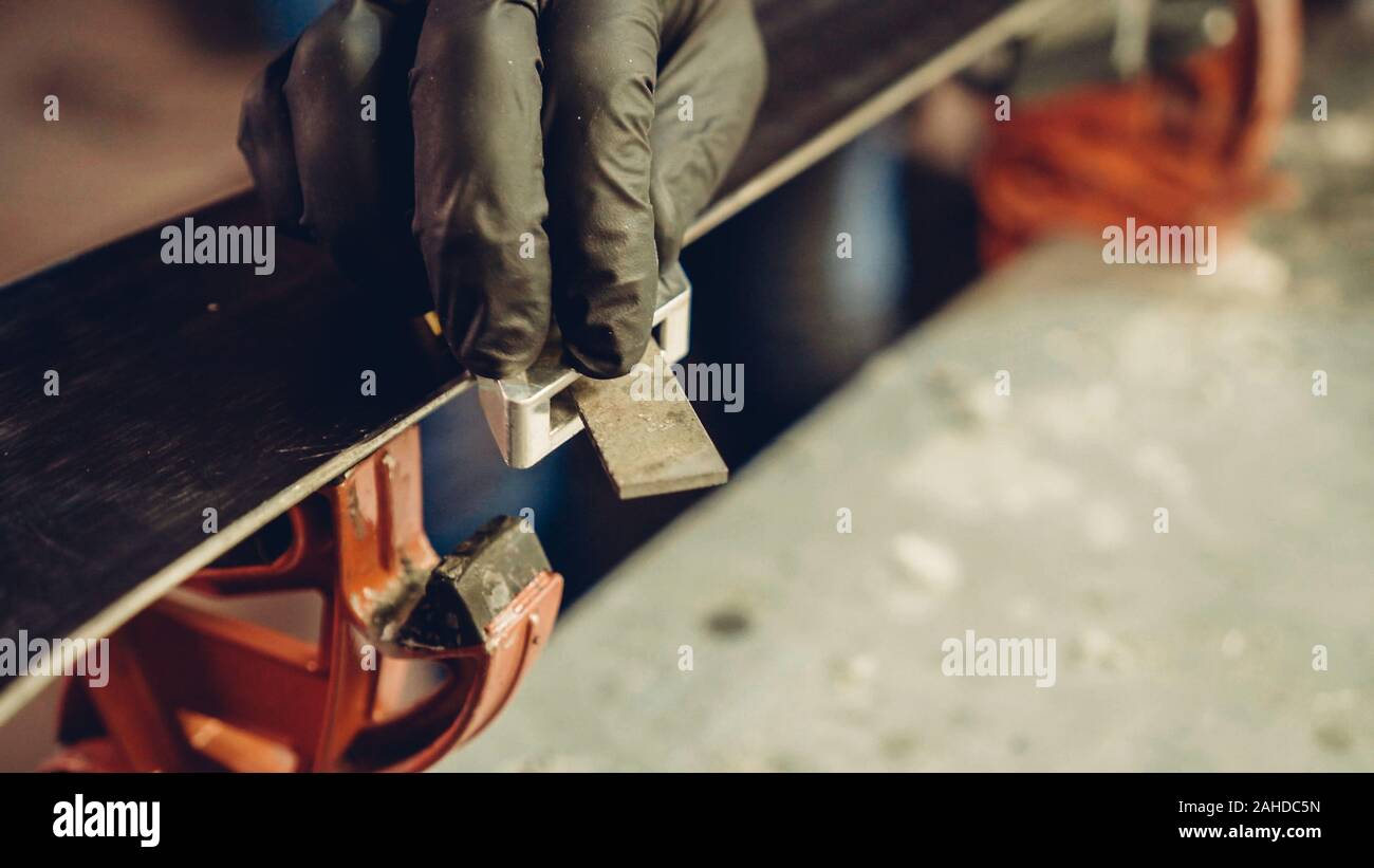 Male worker of ski service workshop doing sharpening and repair of skis ...