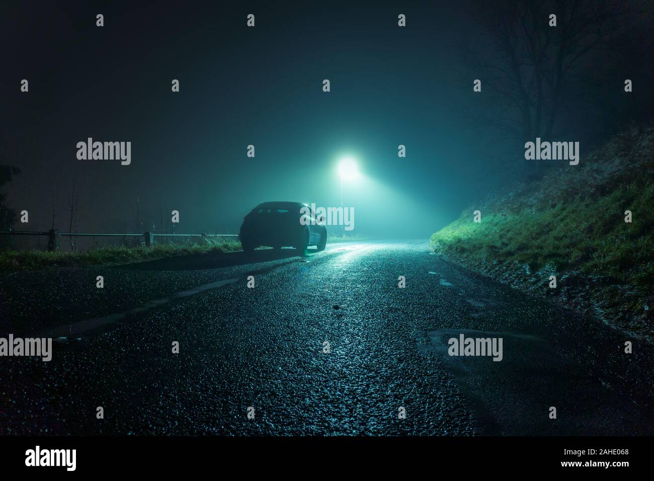 A lone car, parked on the side of the road, underneath a street light ...