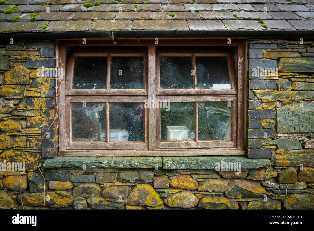 A brown plain frame window of a house made of slate covered with moss ...