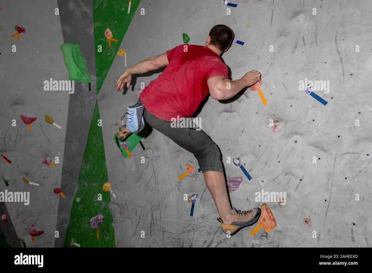 Rock climber man hanging on a bouldering climbing wall, inside on ...