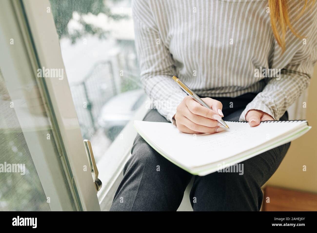 Cropped image of creative young woman sitting on window sill and ...