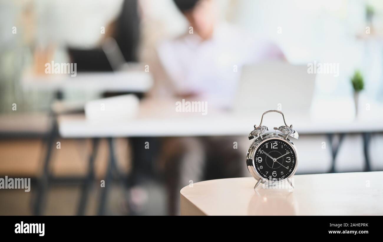 Alarm clock on table with office room blur background Stock Photo - Alamy