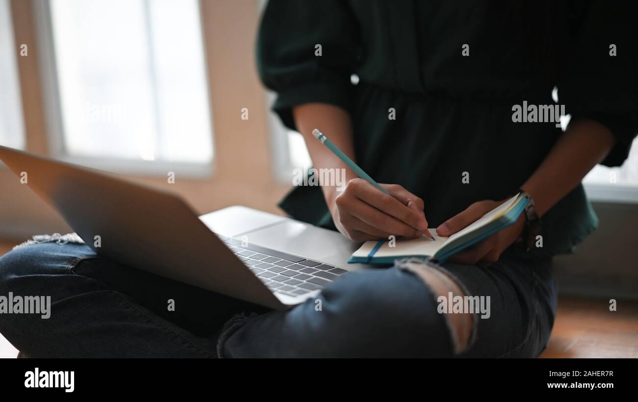 Closeup woman writing notepad and put laptop on leg with sitting on the ...