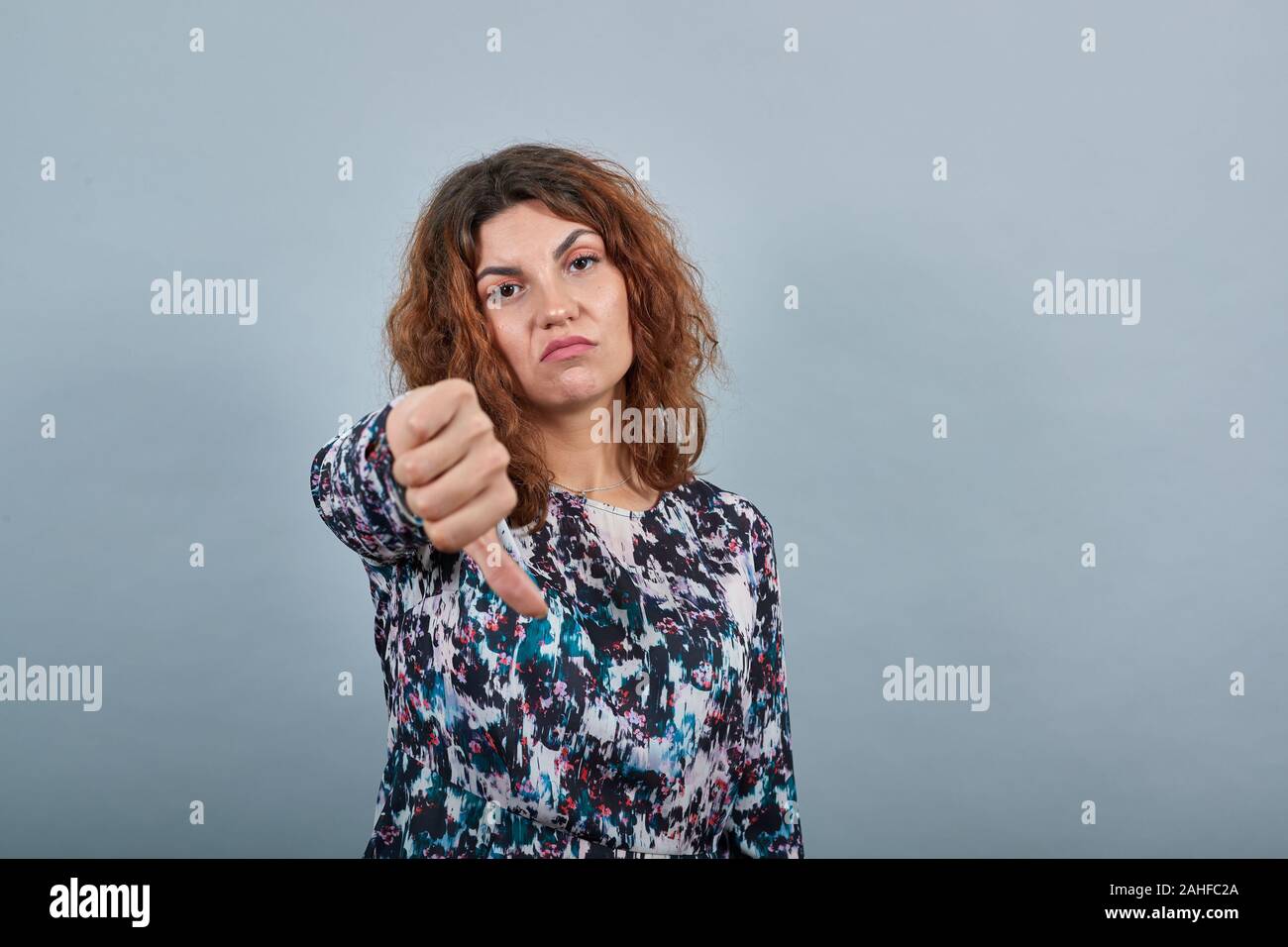 Pretty caucasian young woman keeping thumb down, looking disappointed ...