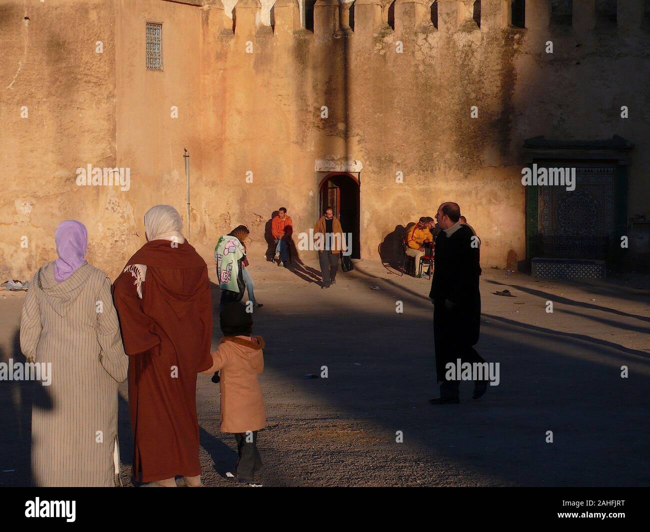 People outside the ancient walls of Fez Morocco in warm evening light ...