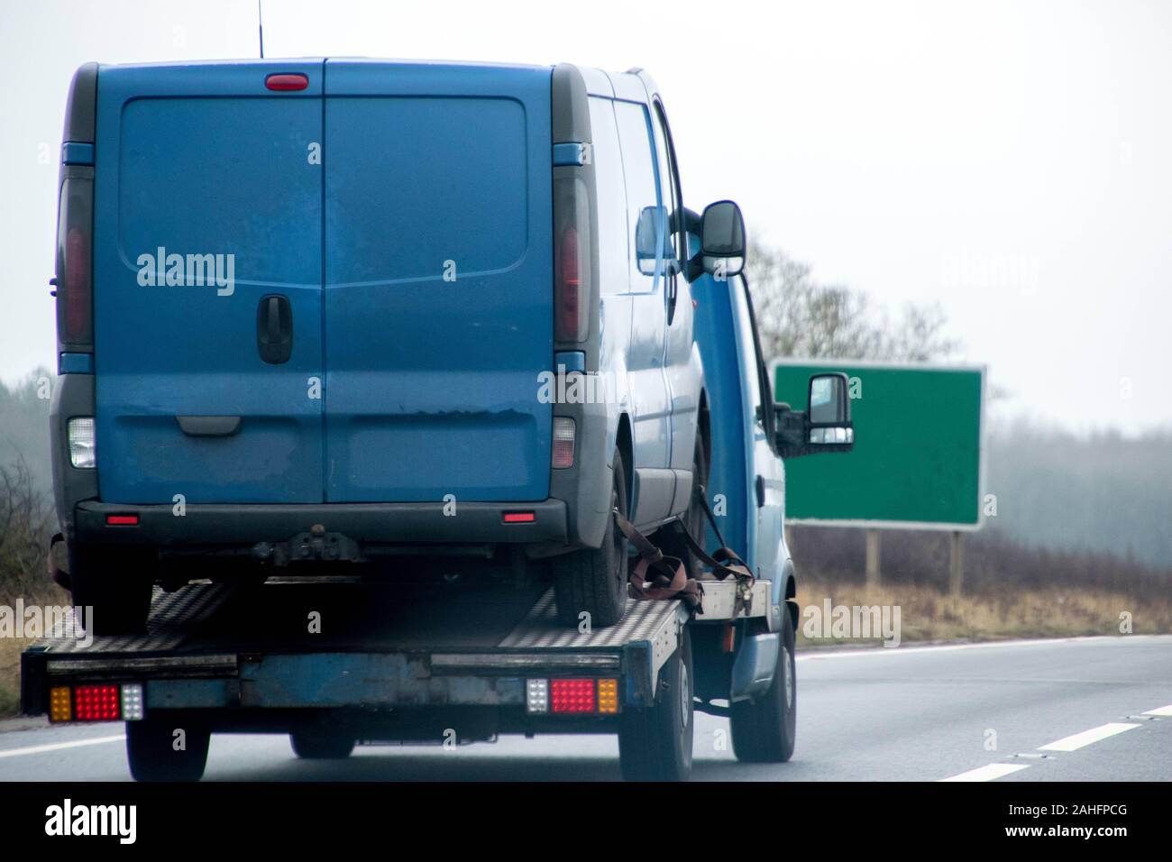 A blue breakdown vehicle carrying a blue van on the back. The view from ...