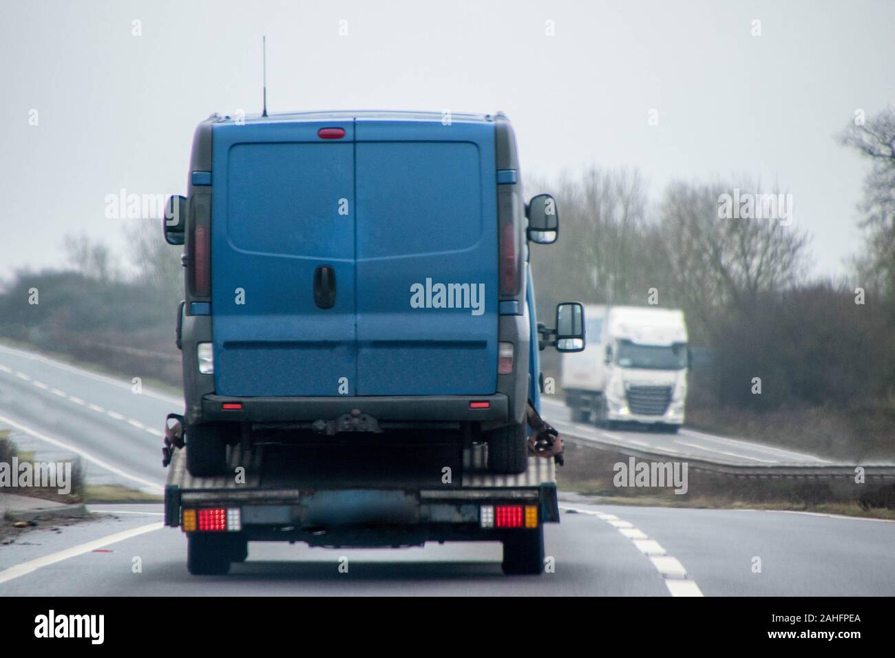 A blue breakdown vehicle carrying a blue van on the back. The view from ...