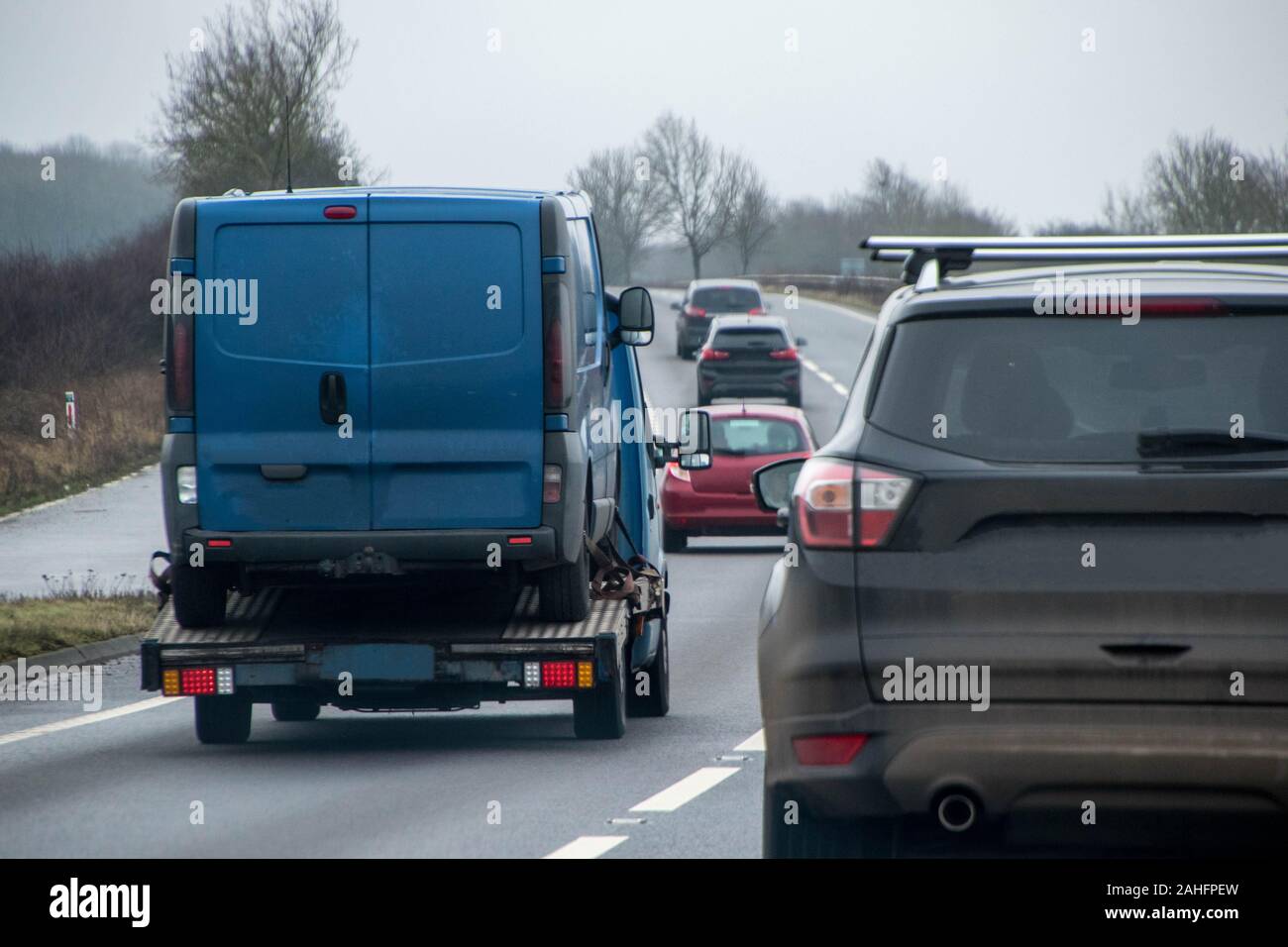 A blue breakdown vehicle carrying a blue van on the back. The view from ...