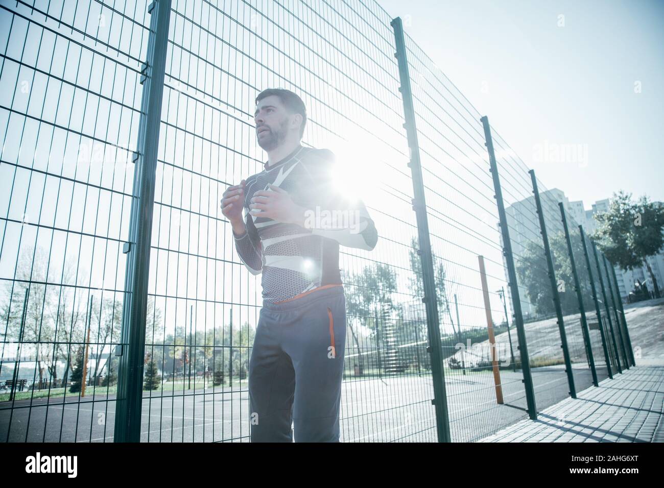 Bearded sportsman jumping near the chain link fence at the sports ...