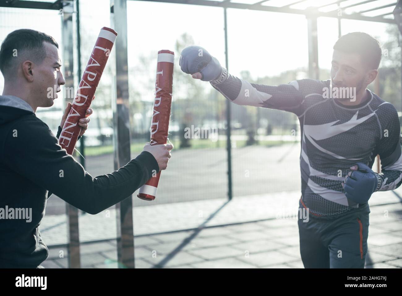 Active sportsman mastering his punch and his trainer holding boxing ...