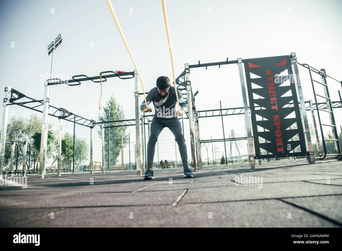 Strong serious sportsman bending his back while pulling rubber ropes ...