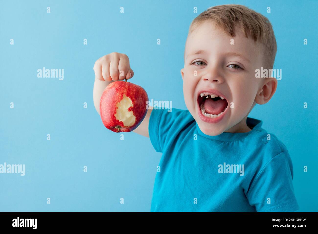 Baby child holding and eating red apple on blue background, food, diet ...