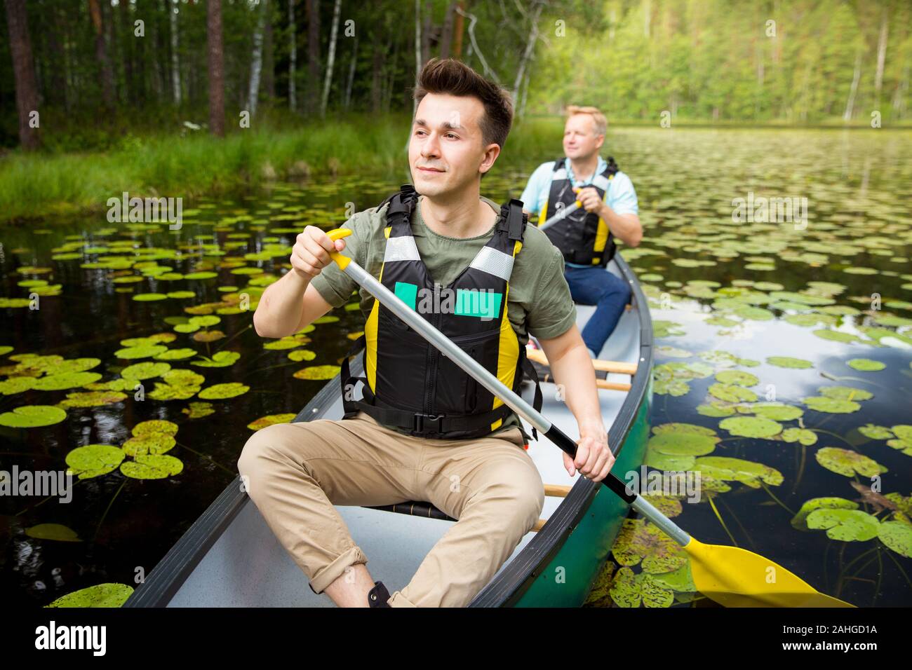 Two men in life vests canoeing in forest lake. Water surface covered ...