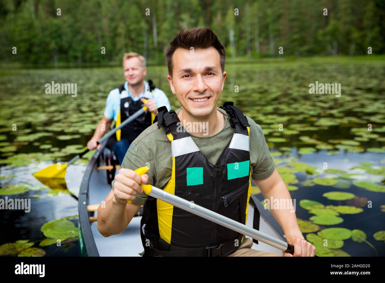 Two men in life vests canoeing in forest lake. Water surface covered ...