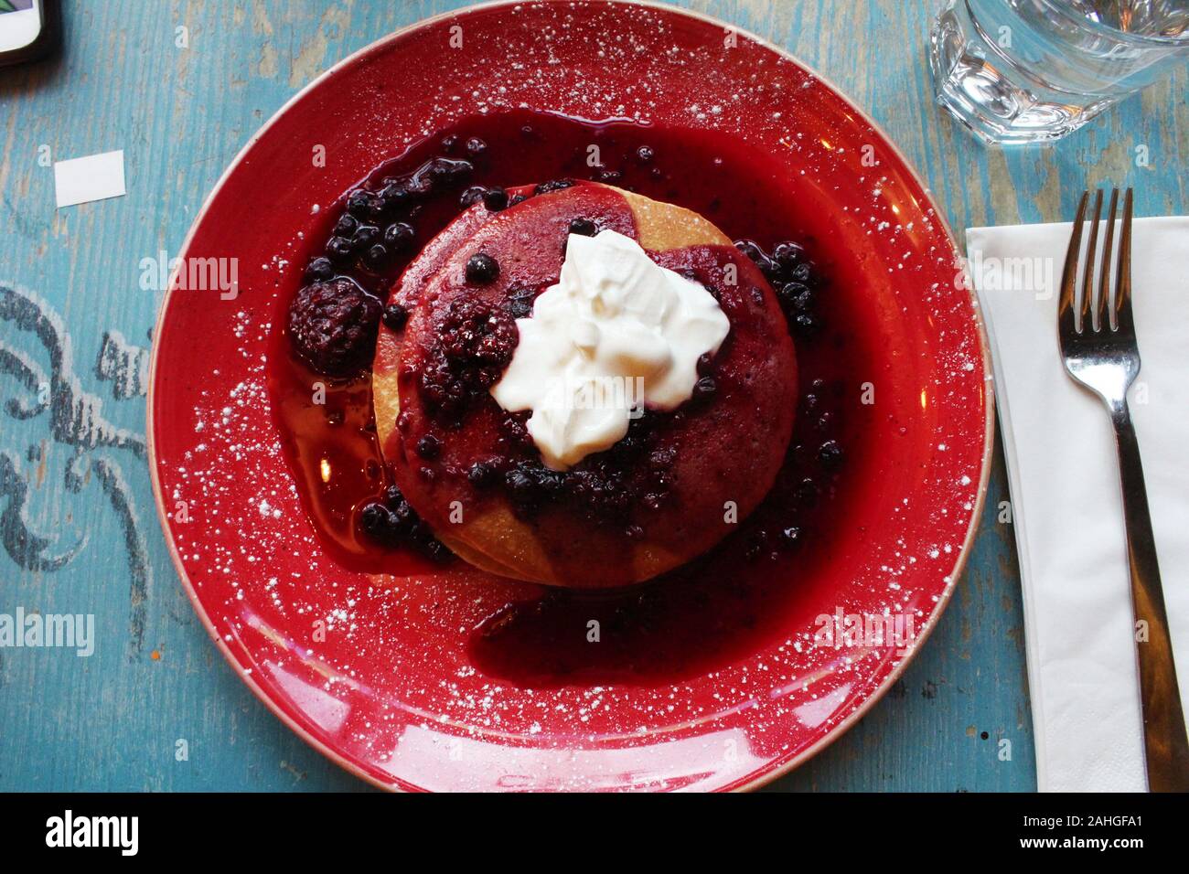 A red plate of stacked pancakes with raspberries, cranberries and ...