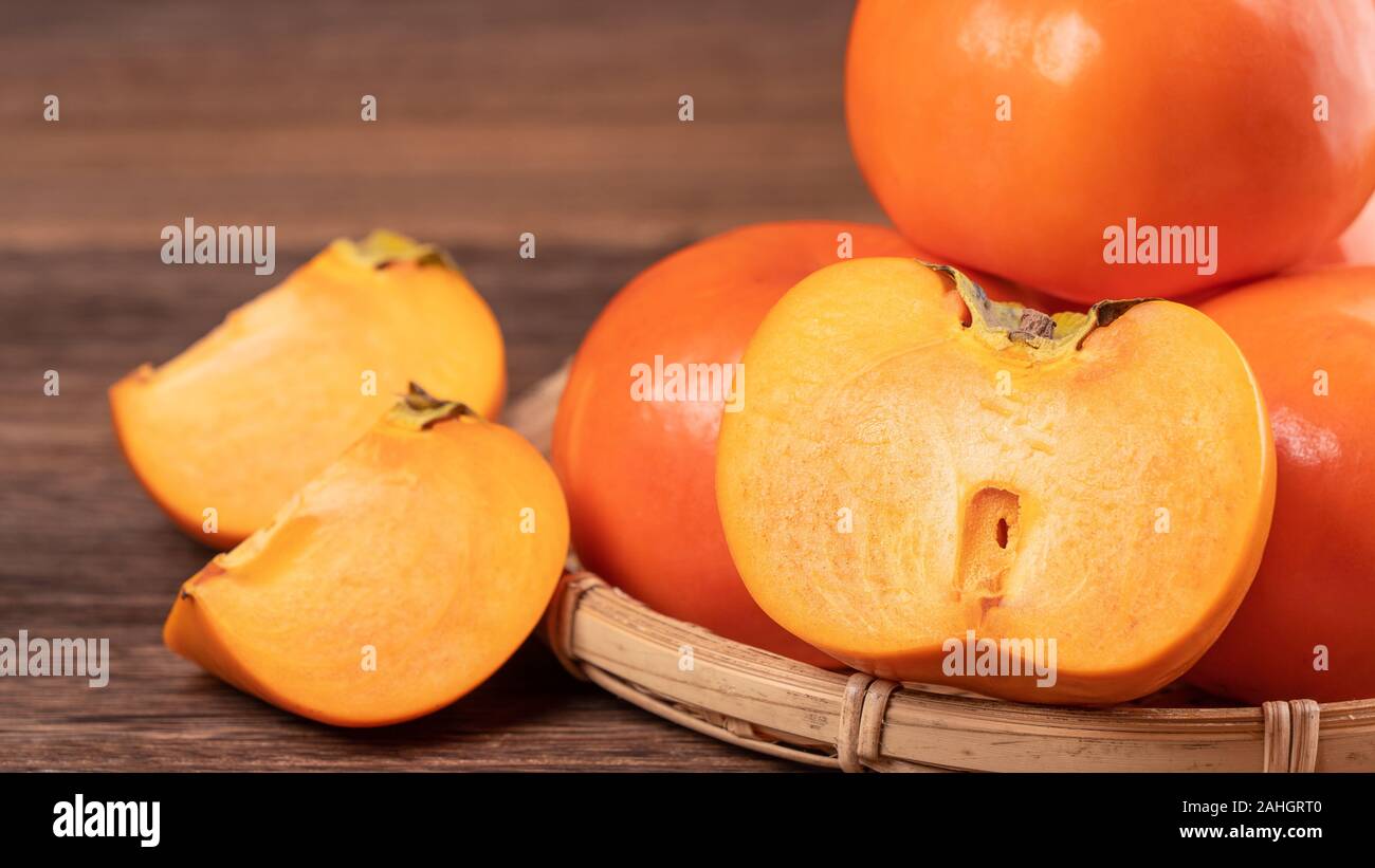 Fresh, beautiful orange color persimmon kaki on bamboo sieve over dark ...