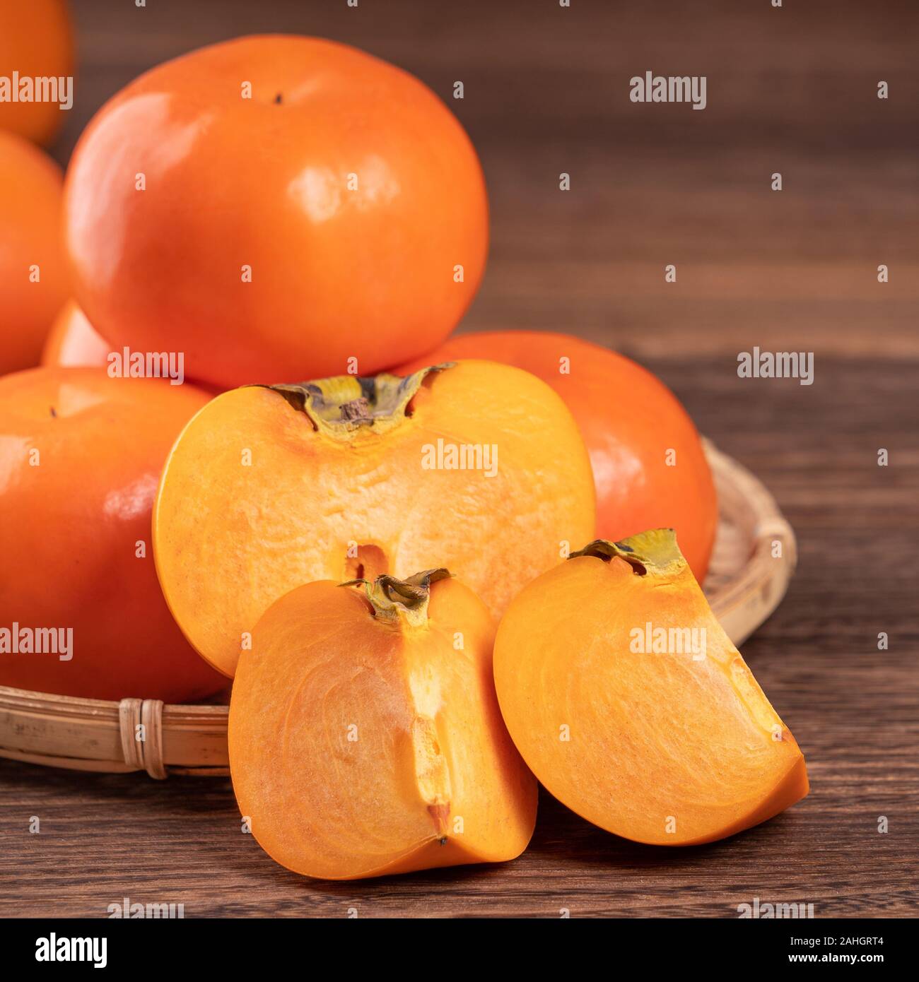 Fresh, beautiful orange color persimmon kaki on bamboo sieve over dark ...