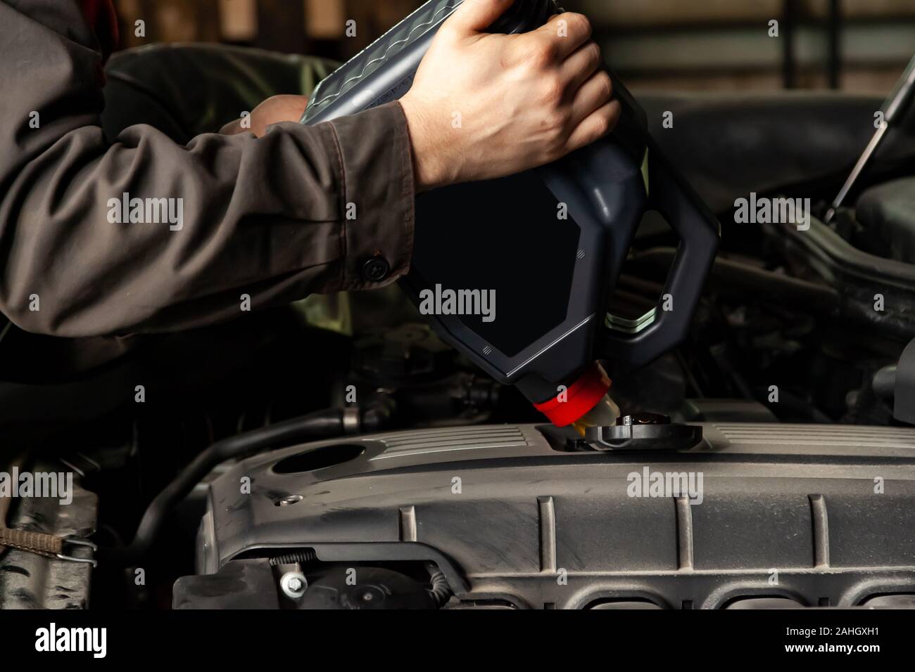 A male worker pours motor oil into a car engine from a gray canister ...