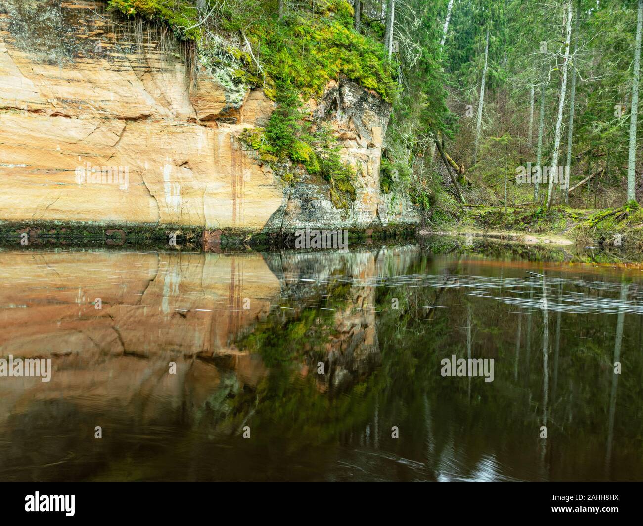 a landscape with a steep river and caves on a sandstone cliff, a cloudy ...