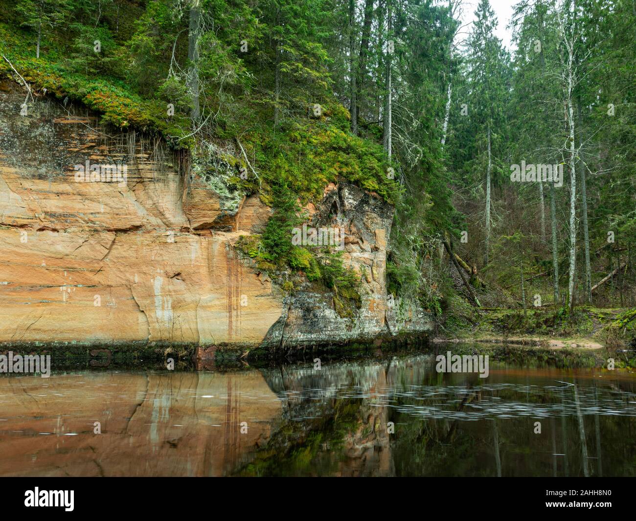 a landscape with a steep river and caves on a sandstone cliff, a cloudy ...