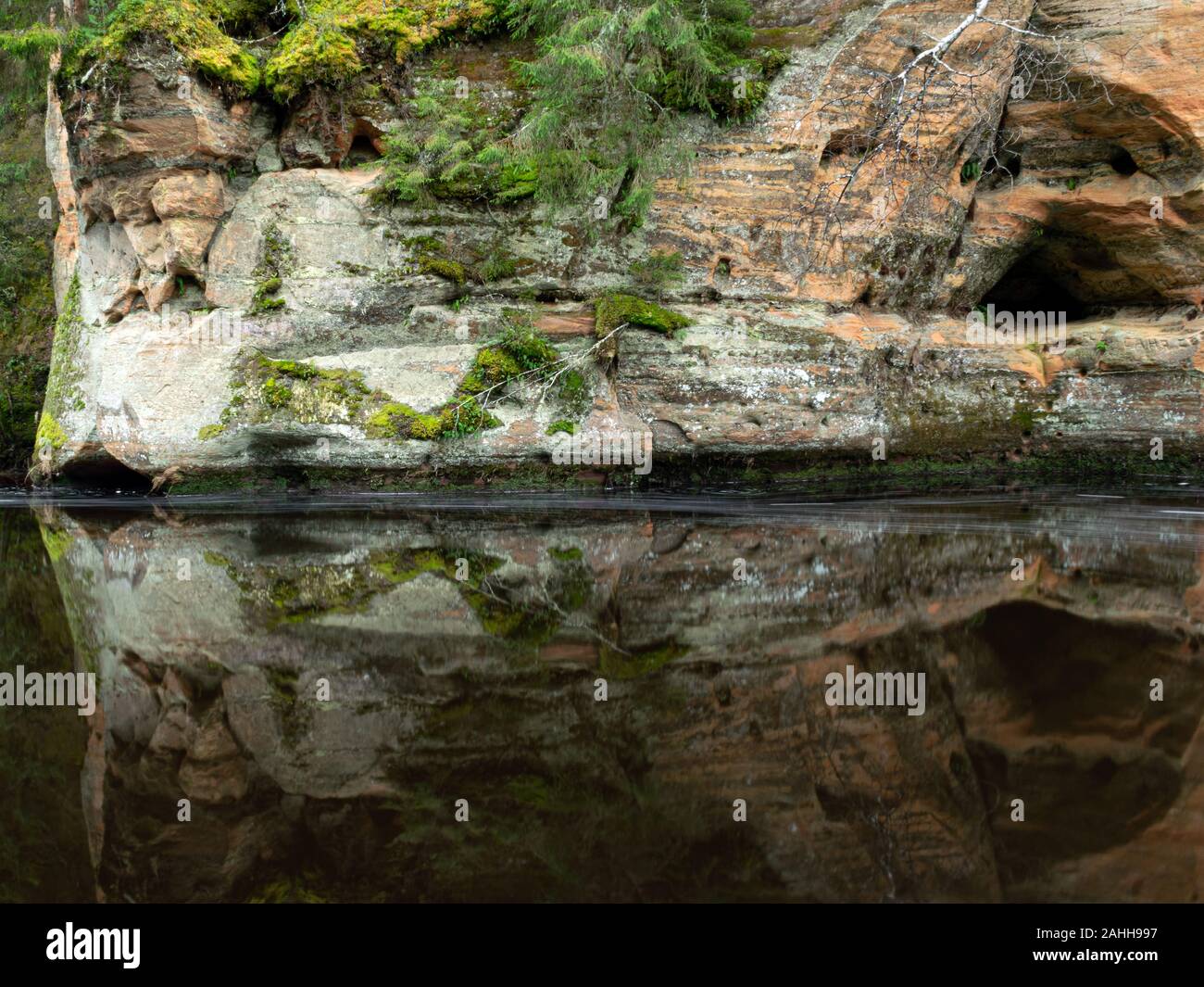 a landscape with a steep river and caves on a sandstone cliff, a cloudy ...
