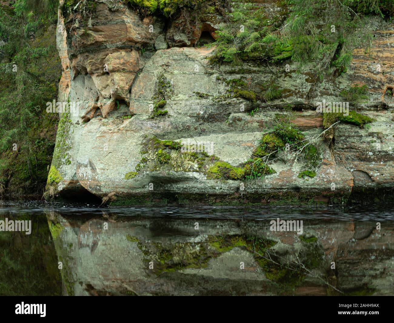 a landscape with a steep river and caves on a sandstone cliff, a cloudy ...