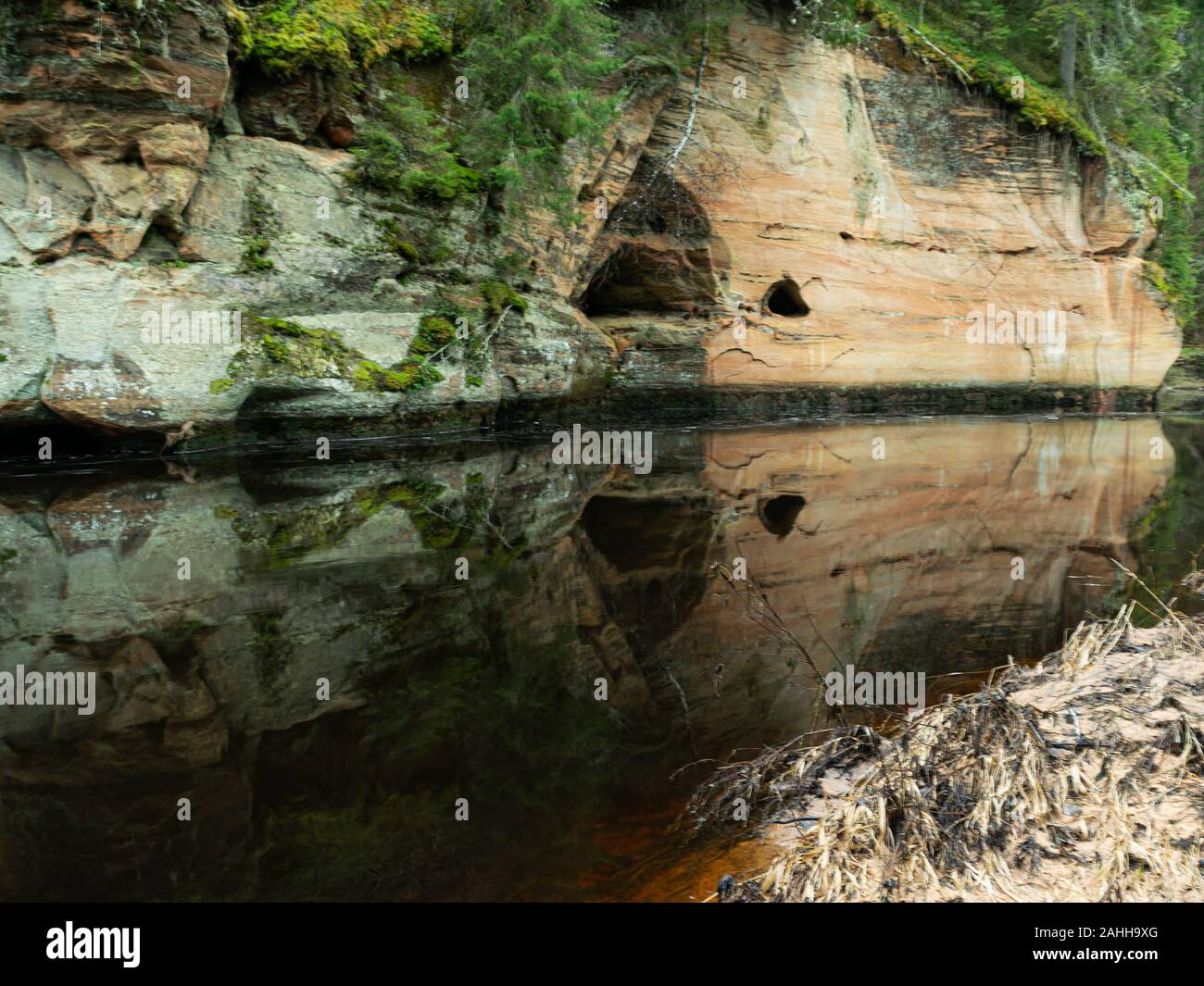 a landscape with a steep river and caves on a sandstone cliff, a cloudy ...