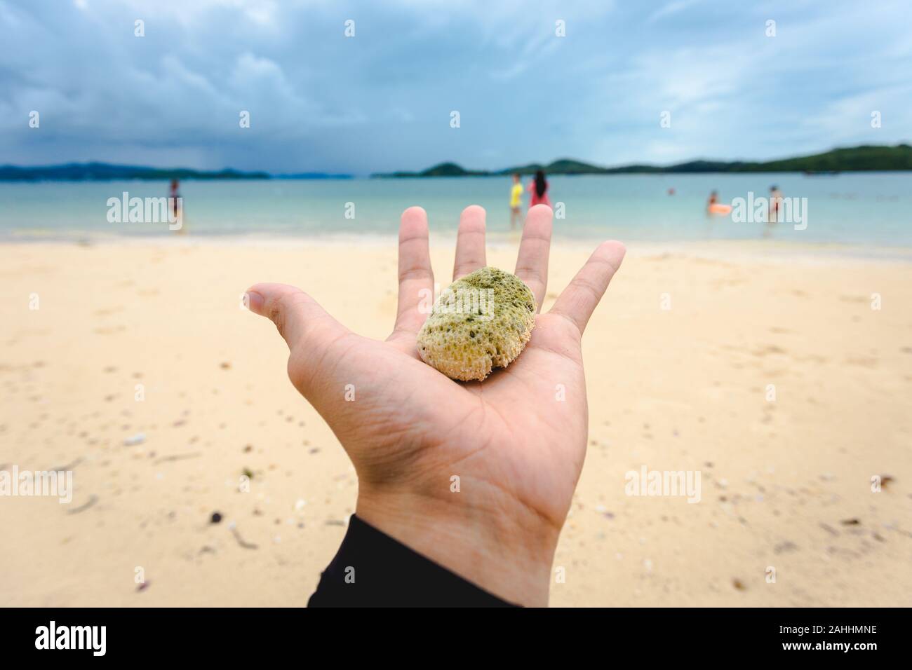 small coral ball on a hand with seaside background and people around ...