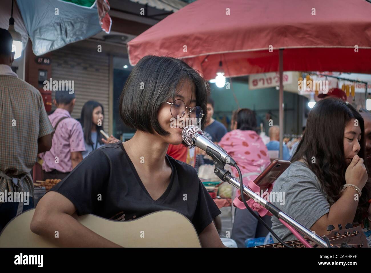 Young busker girl singing with a microphone and playing a guitar at a ...
