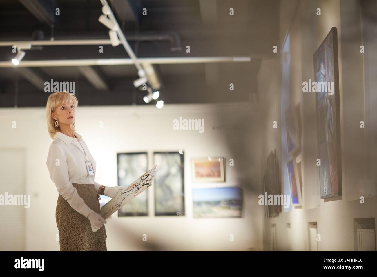 Wide angle portrait of female art expert appraising paintings in modern ...
