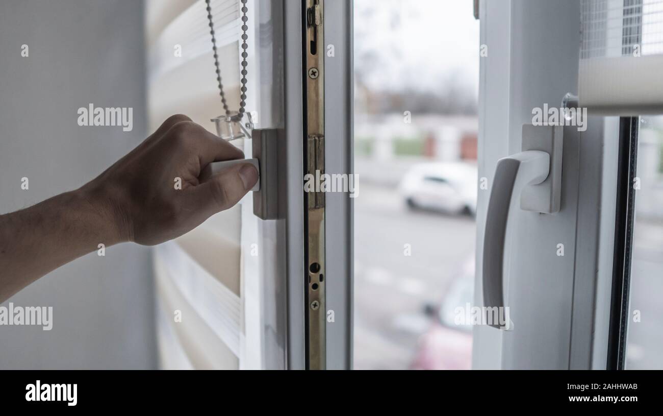Man holding window handle on a plastic window with white fabric roller ...