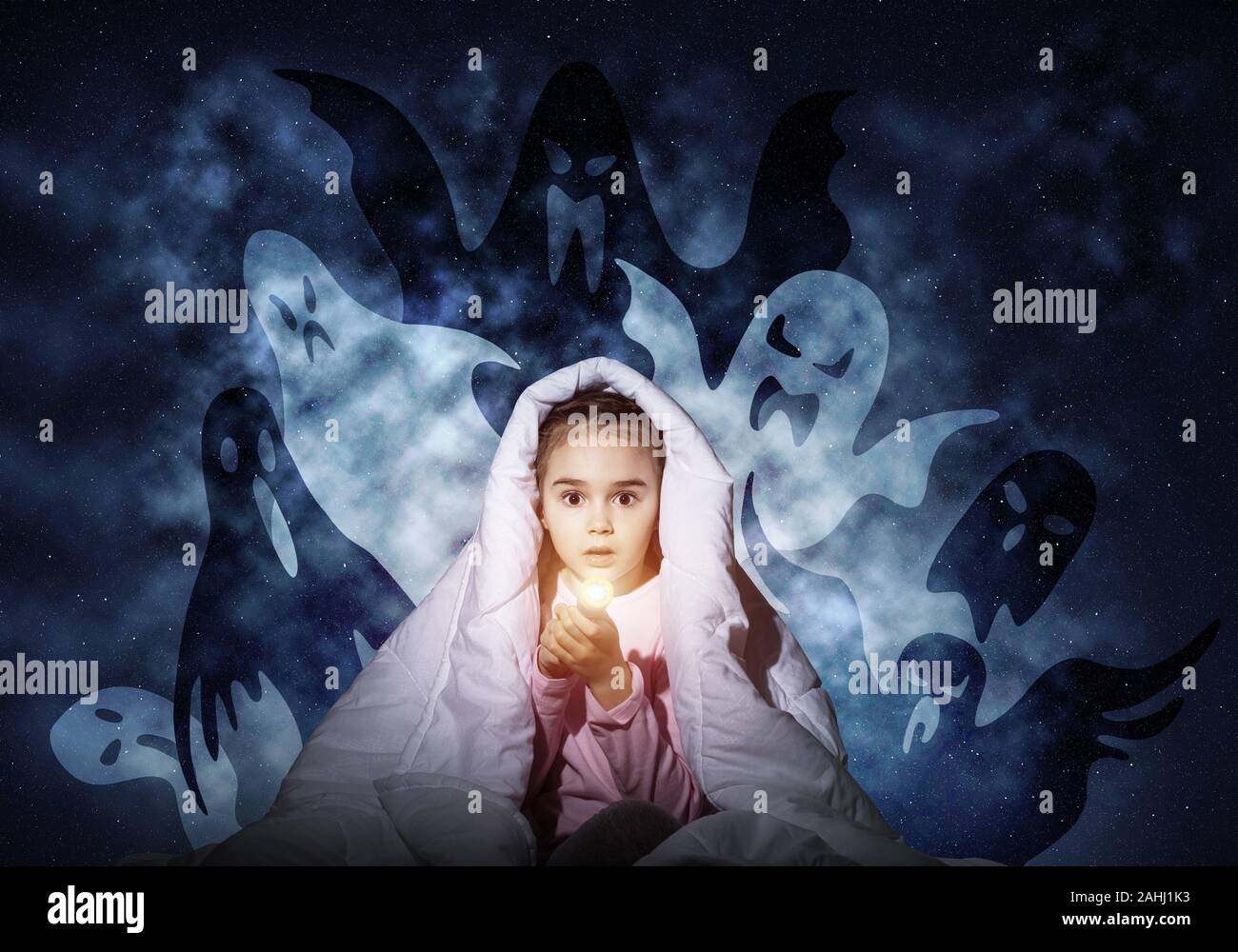 Scared girl with flashlight hiding under blanket from imaginary ghosts ...