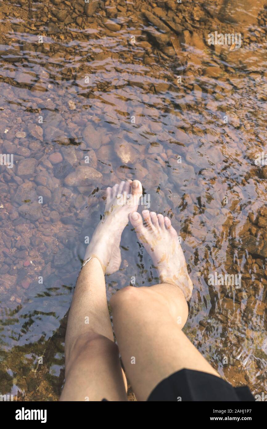 woman in black skirt put feet in water, have stone under river with ...