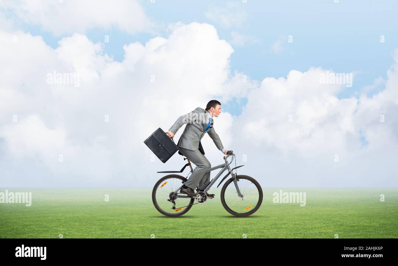 Young man riding bicycle on green grass. Businessman on bike hurry to ...