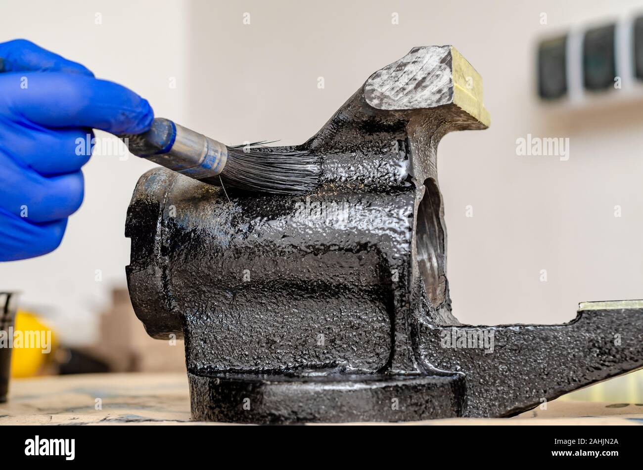 Hand in blue rubber gloves paints metal parts of an old vise with black ...