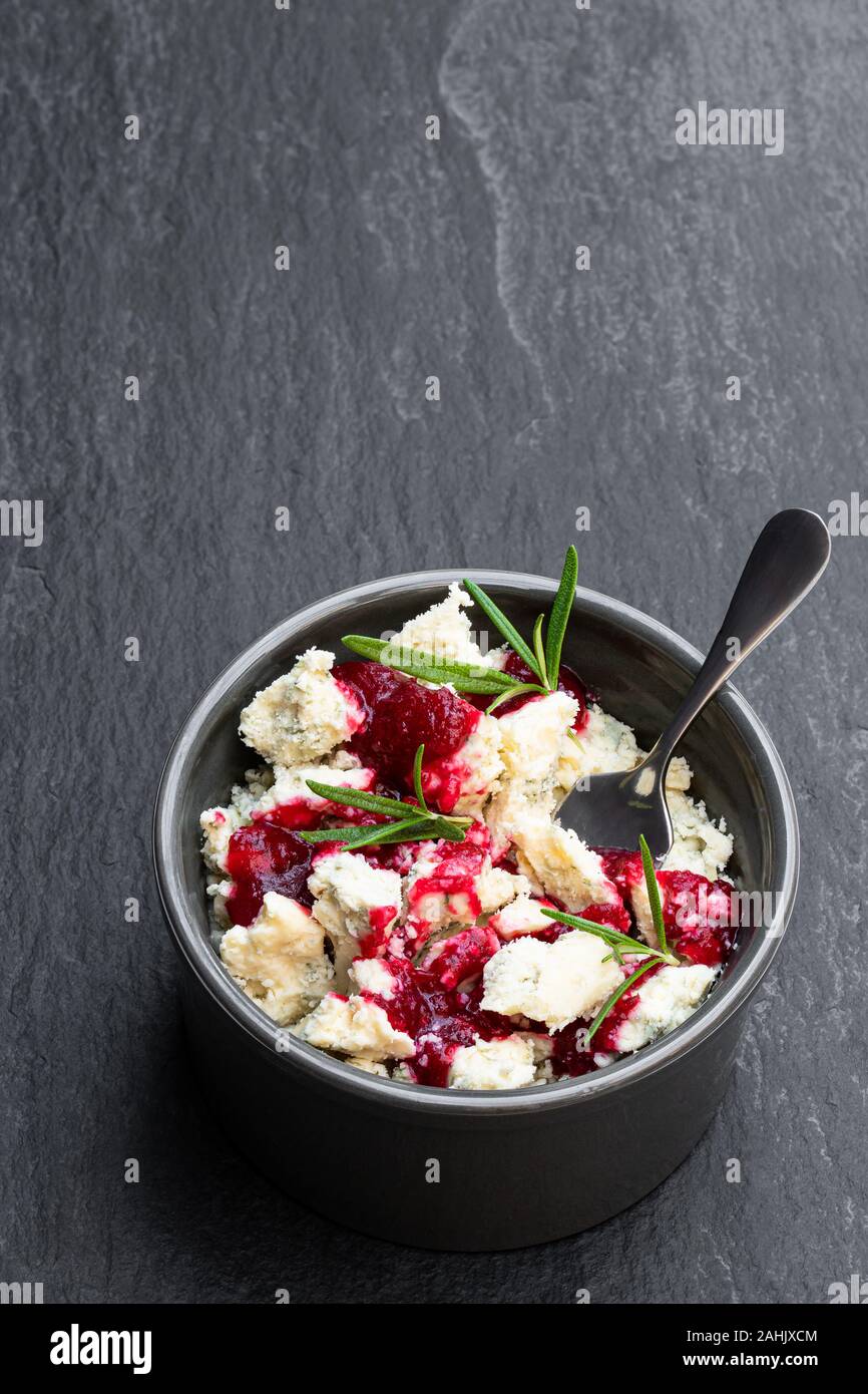 Potted aged Blue stilton cheese with cranberry sauce on black stone ...