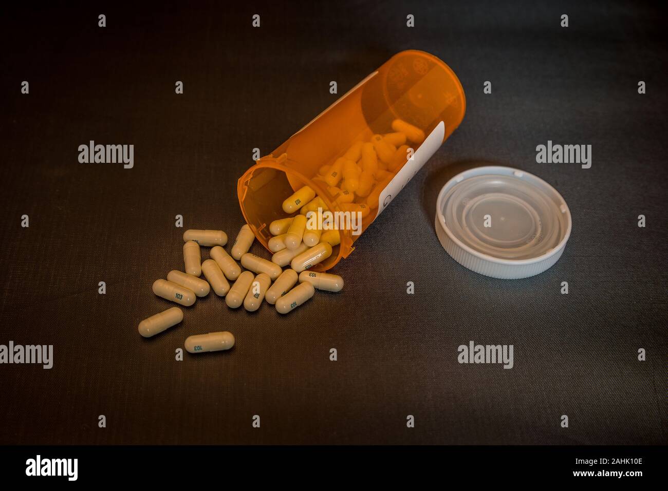 Prescription capsules spilling out of a orange bottle onto a black ...