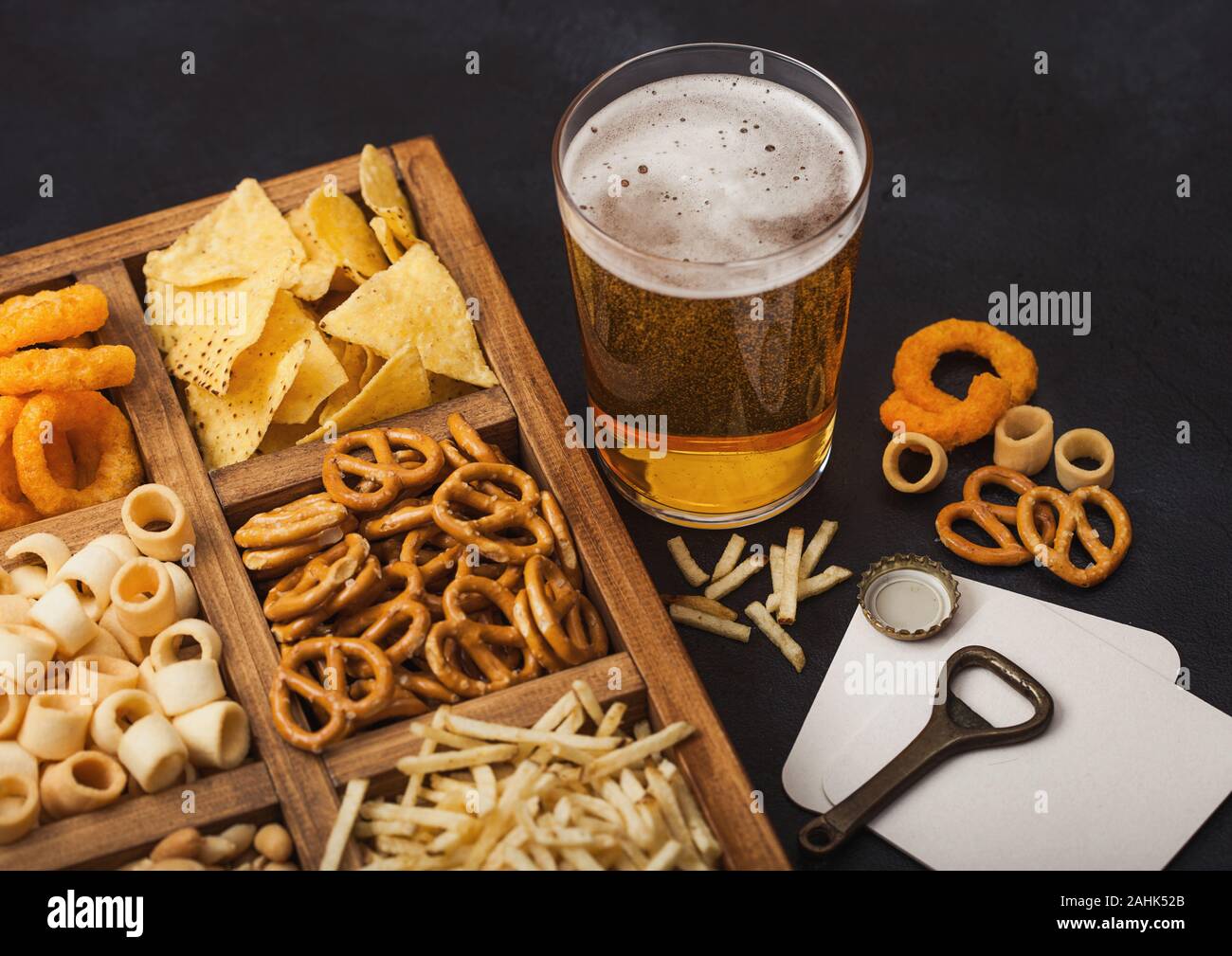 Glass of craft lager beer and opener with box of snacks on dark ...