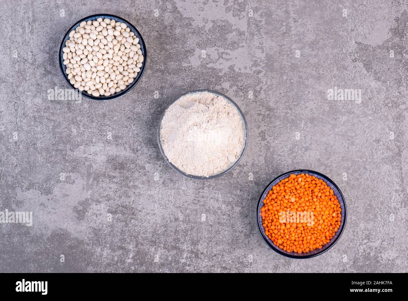 White beans, red lentils and flour on a textured grey background, empty ...
