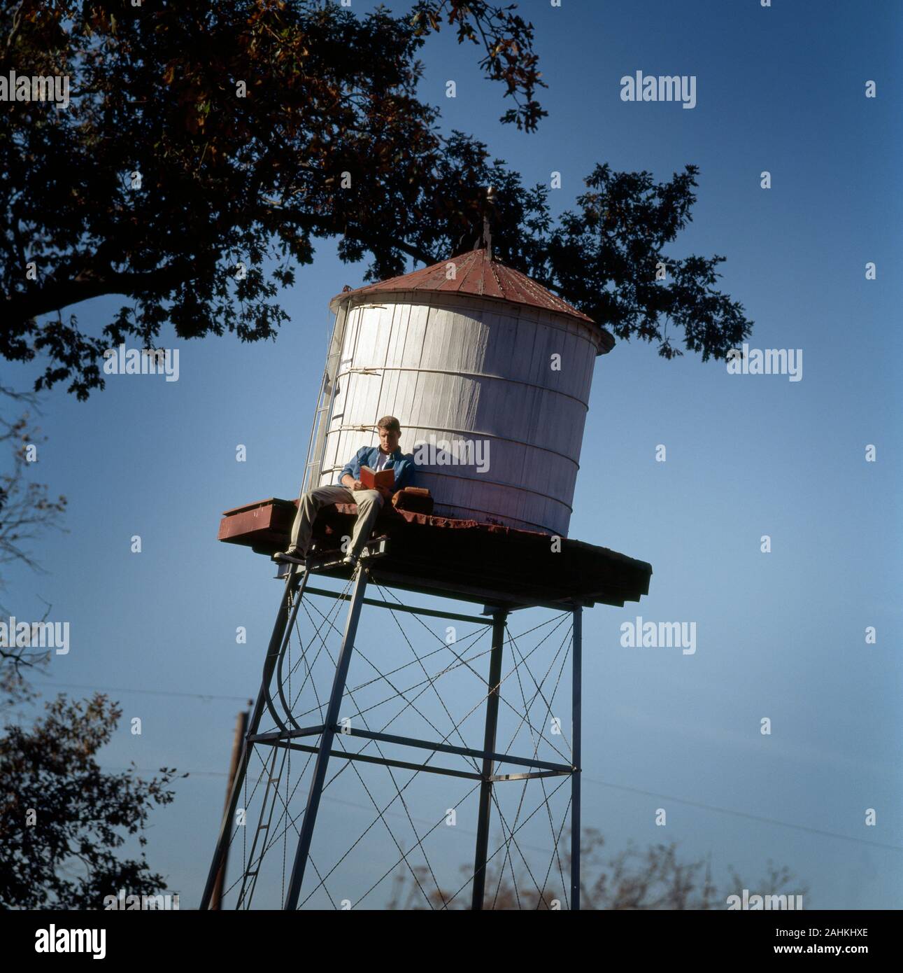 Young man reading a book while sitting up a water tower in the country ...