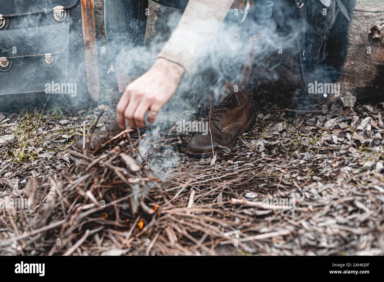 A stock photo of a man in nature sitting by a small fire, warming ...