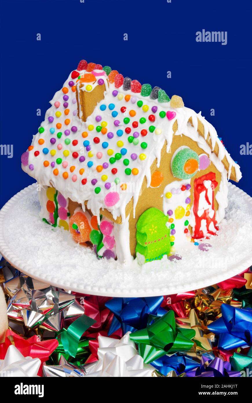Decorated gingerbread house on a white cake stand. Powdered sugar is ...
