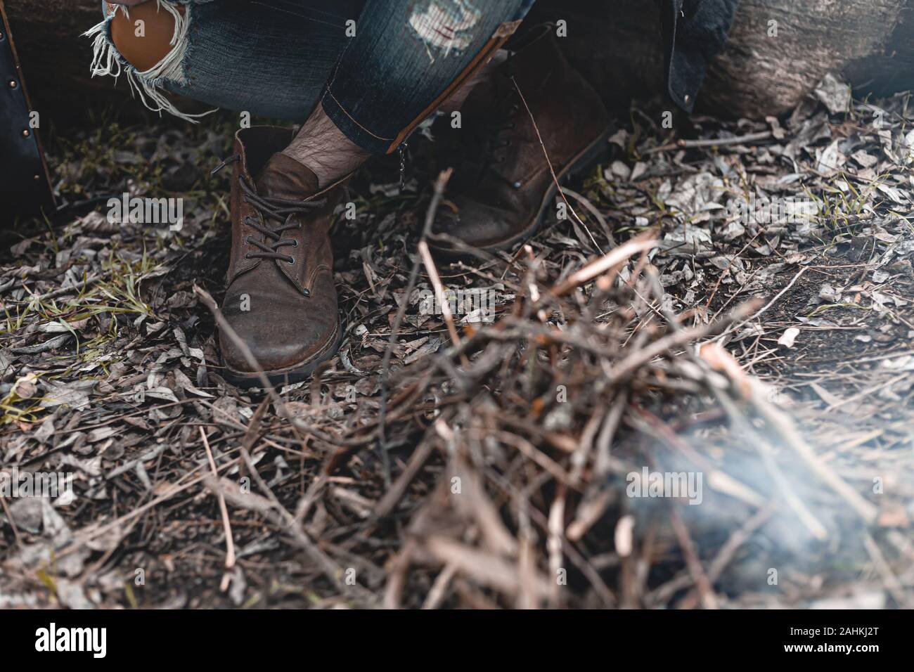 A stock photo of a man in nature sitting by a small fire, warming ...