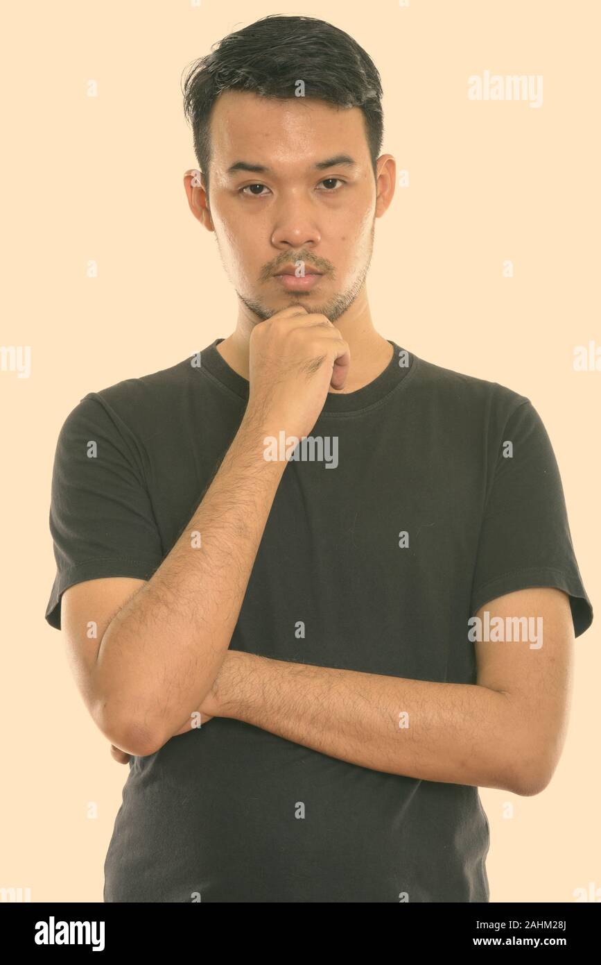 Studio shot of young Asian man thinking Stock Photo - Alamy