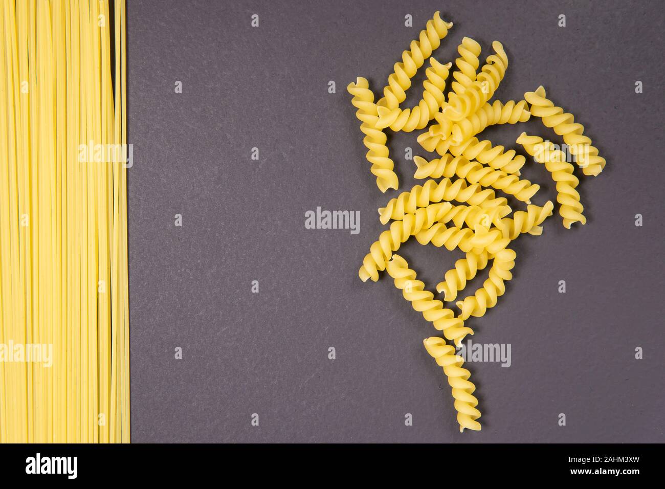 Raw Italian pasta in the form of a spiral and spaghetti on dark grey ...