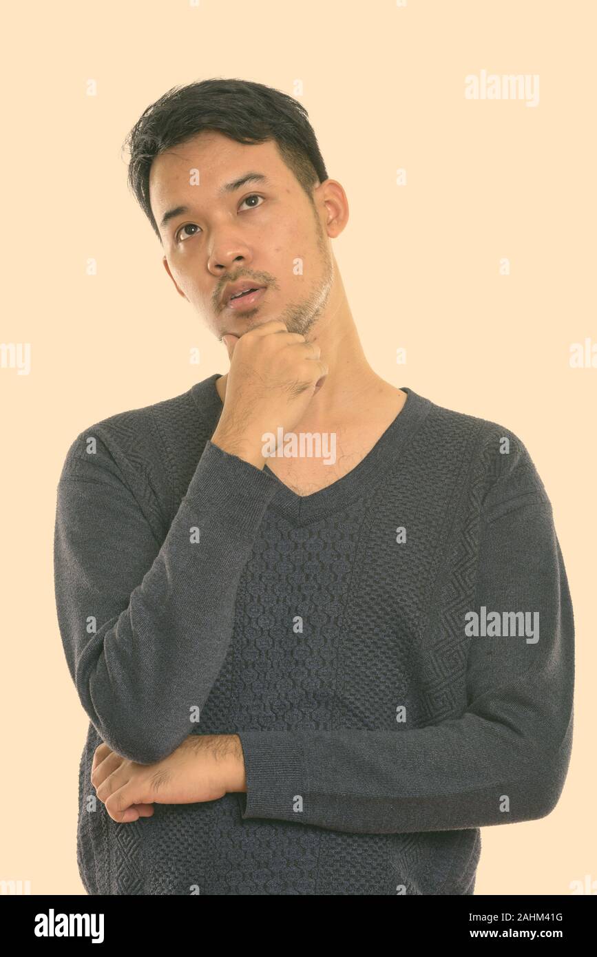 Studio shot of young Asian man thinking while looking up Stock Photo ...
