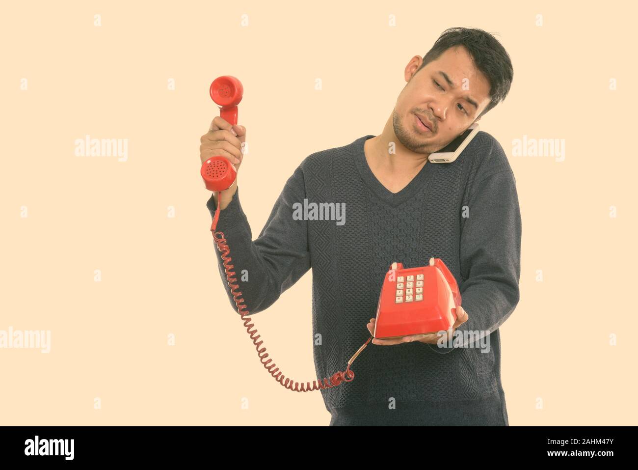 Studio shot of young Asian man giving old telephone while talking on ...