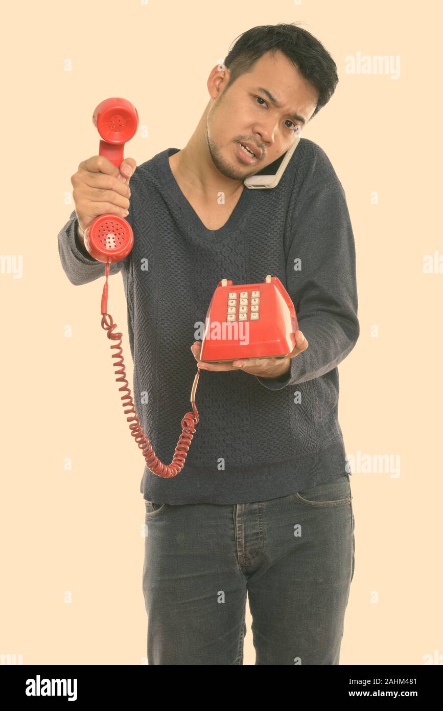 Studio shot of young Asian man standing and giving old telephone while ...